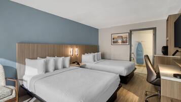 Quarto de hotel com duas camas, uma escrivaninha, uma cadeira e zona de chuveiro.