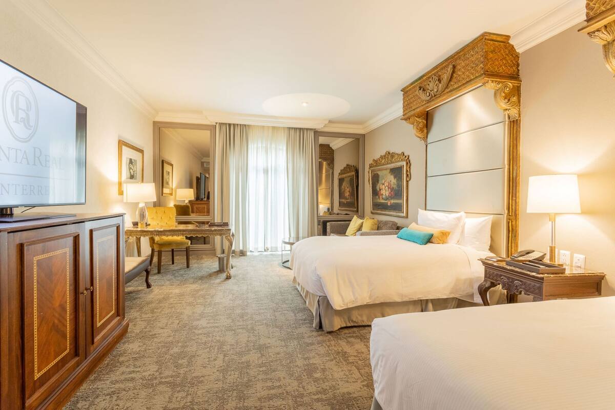 Quarto de hotel com duas camas, uma escrivaninha, televisão e um espelho grande.