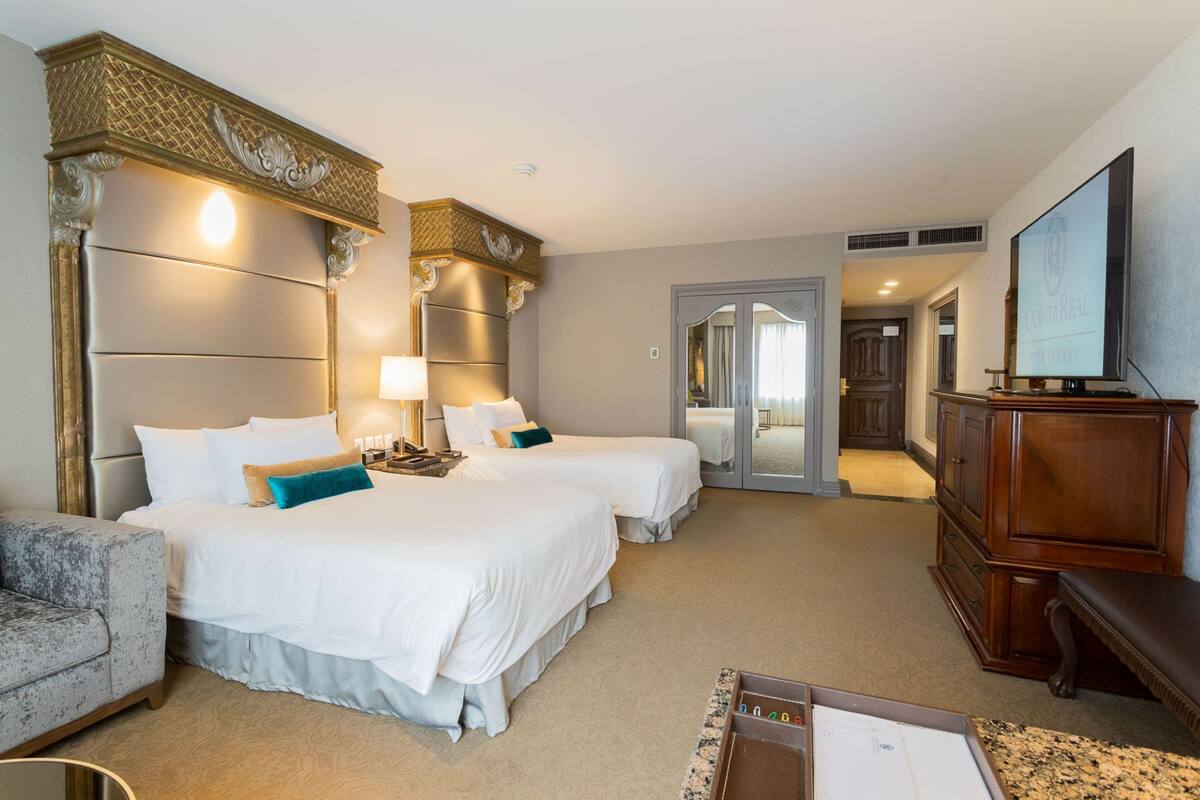 Quarto de hotel com duas camas, um sofá, uma televisão e um espelho grande.