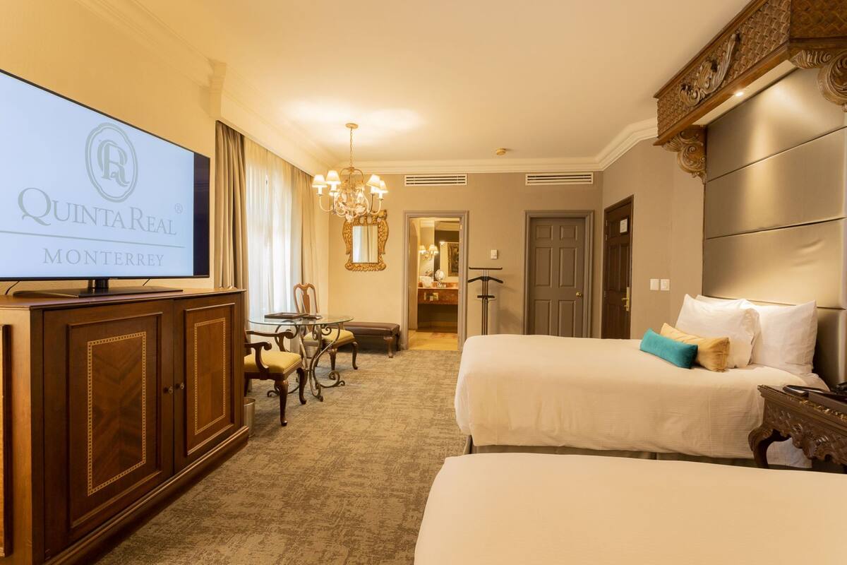 Quarto de hotel com cama, televisão, escrivaninha e cadeira.