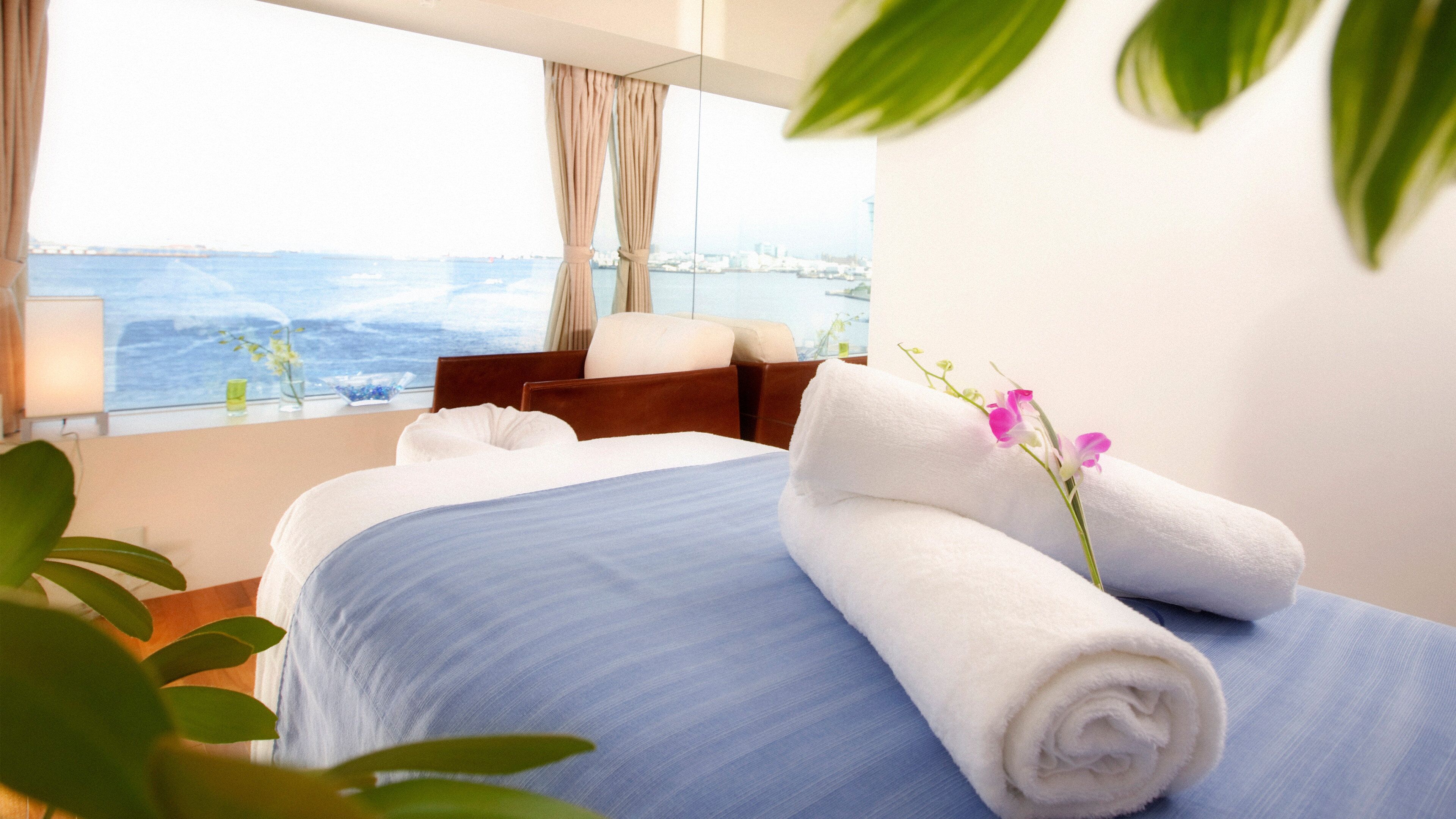 Quarto de hotel com cama, mesa de cabeceira, janela com vista para o mar e uma planta.