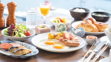 Mesa de café da manhã com diversos pratos, incluindo ovos, salmão, croissants e uma cesta de frutas.