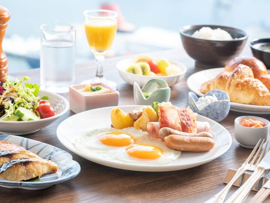 Mesa de café da manhã com diversos pratos, incluindo ovos, salmão, croissants e uma cesta de frutas.