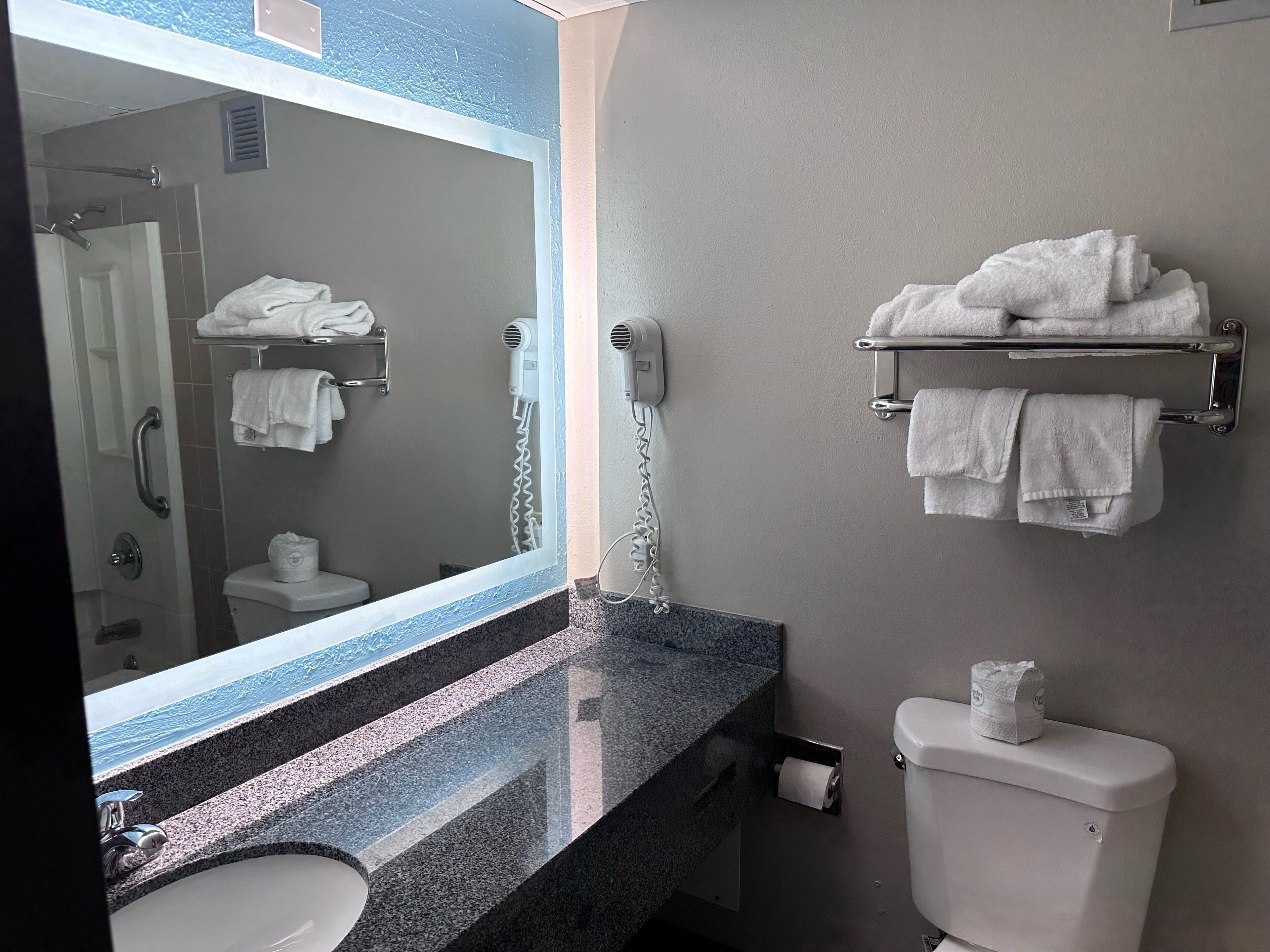 Um banheiro moderno com um espelho grande, bancada de granito, vaso sanitário e porta-toalhas.