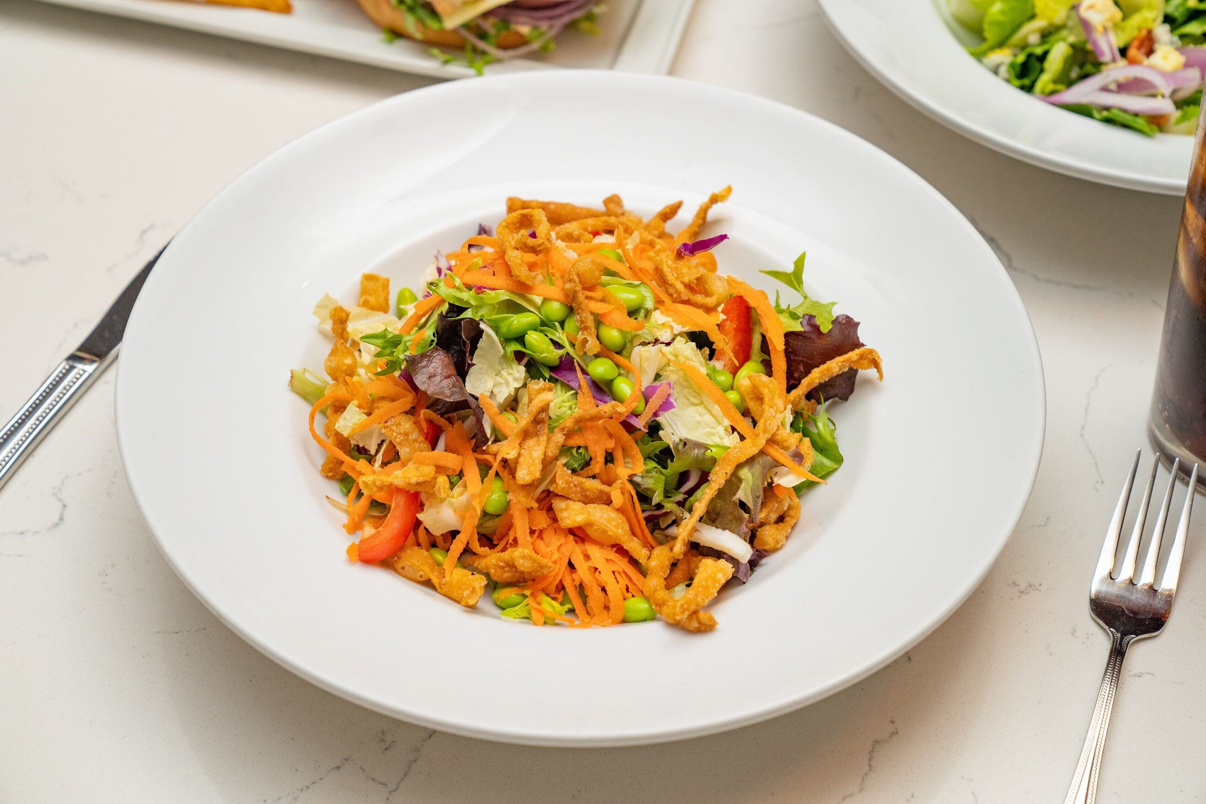 Um prato branco com salada sobre uma mesa de mármore.