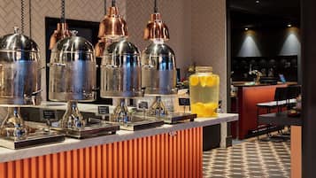 Uma área de bar com dosadores de bebidas em cobre e vidro, um grande pote de vidro com fatias de cítricos e um chão estampado.