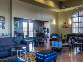 Um hall amplo com sofás, cadeiras, um espaço para café e vista para a rua.