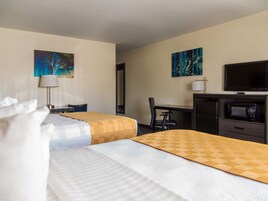Quarto de hotel com duas camas, uma escrivaninha, uma cadeira, uma televisão e um micro-ondas.