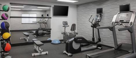 Academia com esteiras, bolas de exercício e um espelho grande.