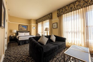 Quarto de hotel com cama, sofá, mesa pequena e mesa de cabeceira.