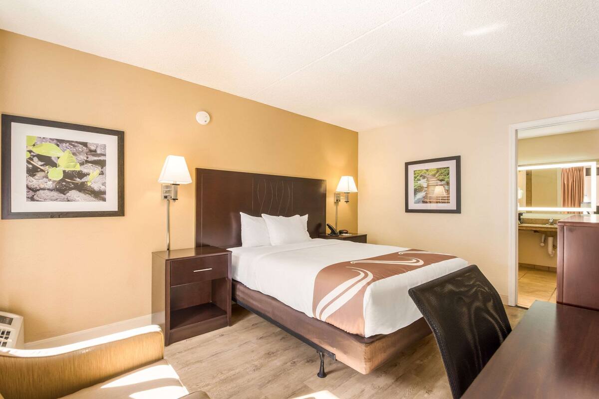 Quarto de hotel com cama, mesas de cabeceira, luminárias, escrivaninha e uma cadeira.