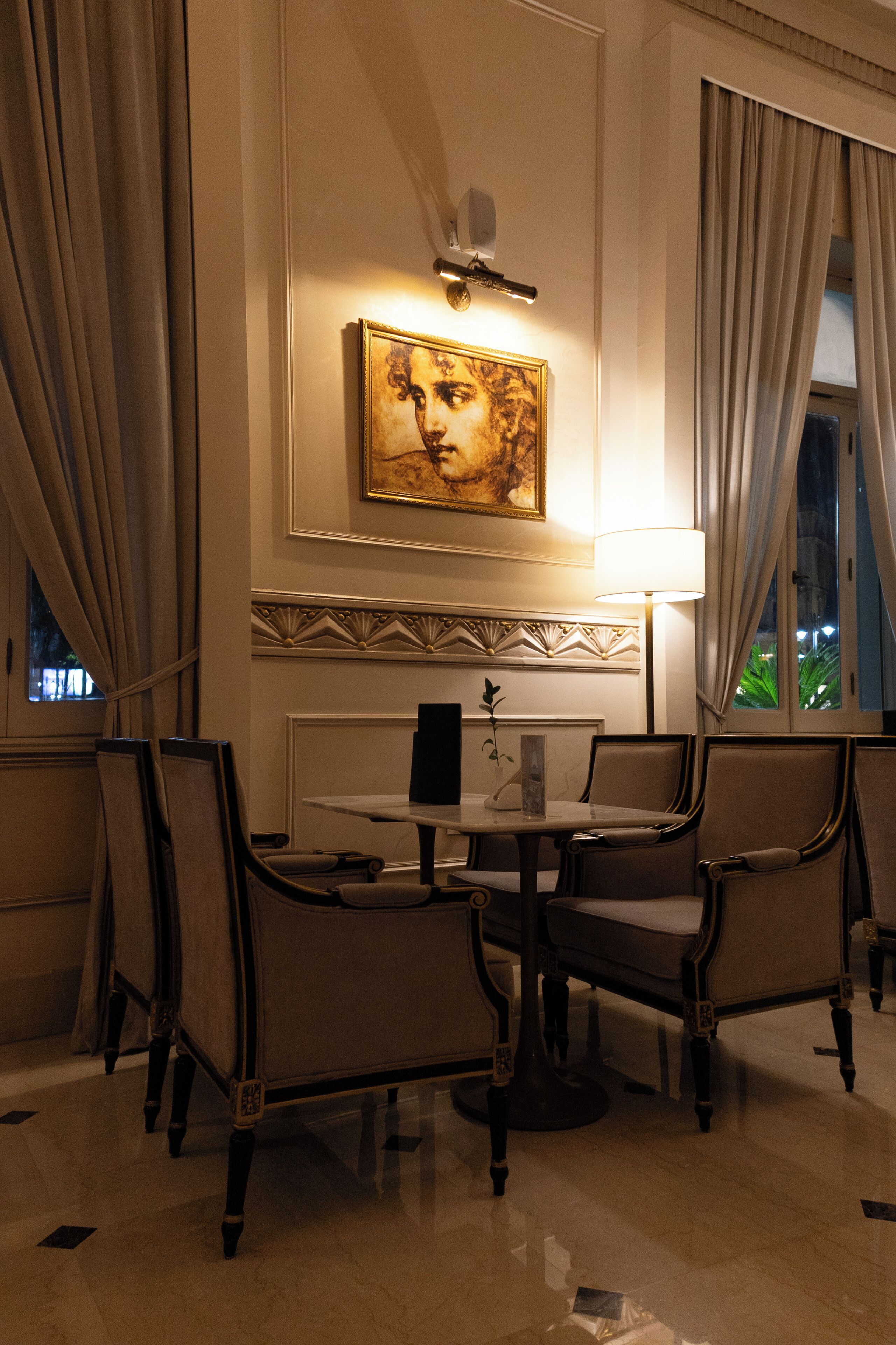 Uma área de refeições com uma mesa e quatro cadeiras, um quadro na parede e uma janela com cortinas.