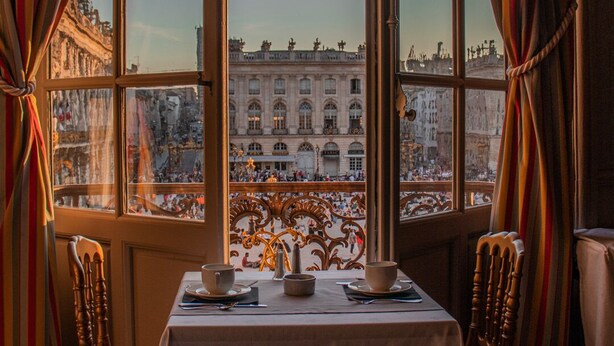 Mesa de jantar com vista para um edifício histórico através de grandes janelas.