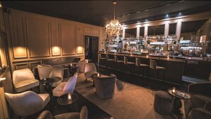 Uma área de bar com assentos, um candelabro e um bar bem abastecido.
