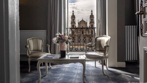 Quarto com duas cadeiras, uma mesa e vista para um edifício histórico através de uma janela.
