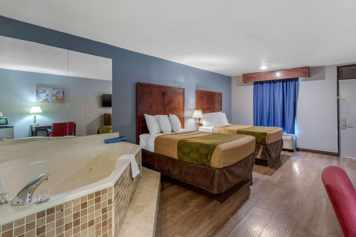 Quarto de hotel com duas camas, uma banheira grande e uma cadeira vermelha.
