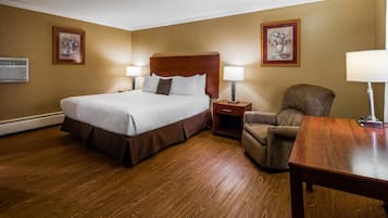 Quarto de hotel com uma cama grande, uma cadeira, uma mesa de cabeceira e duas luminárias fixadas na parede.