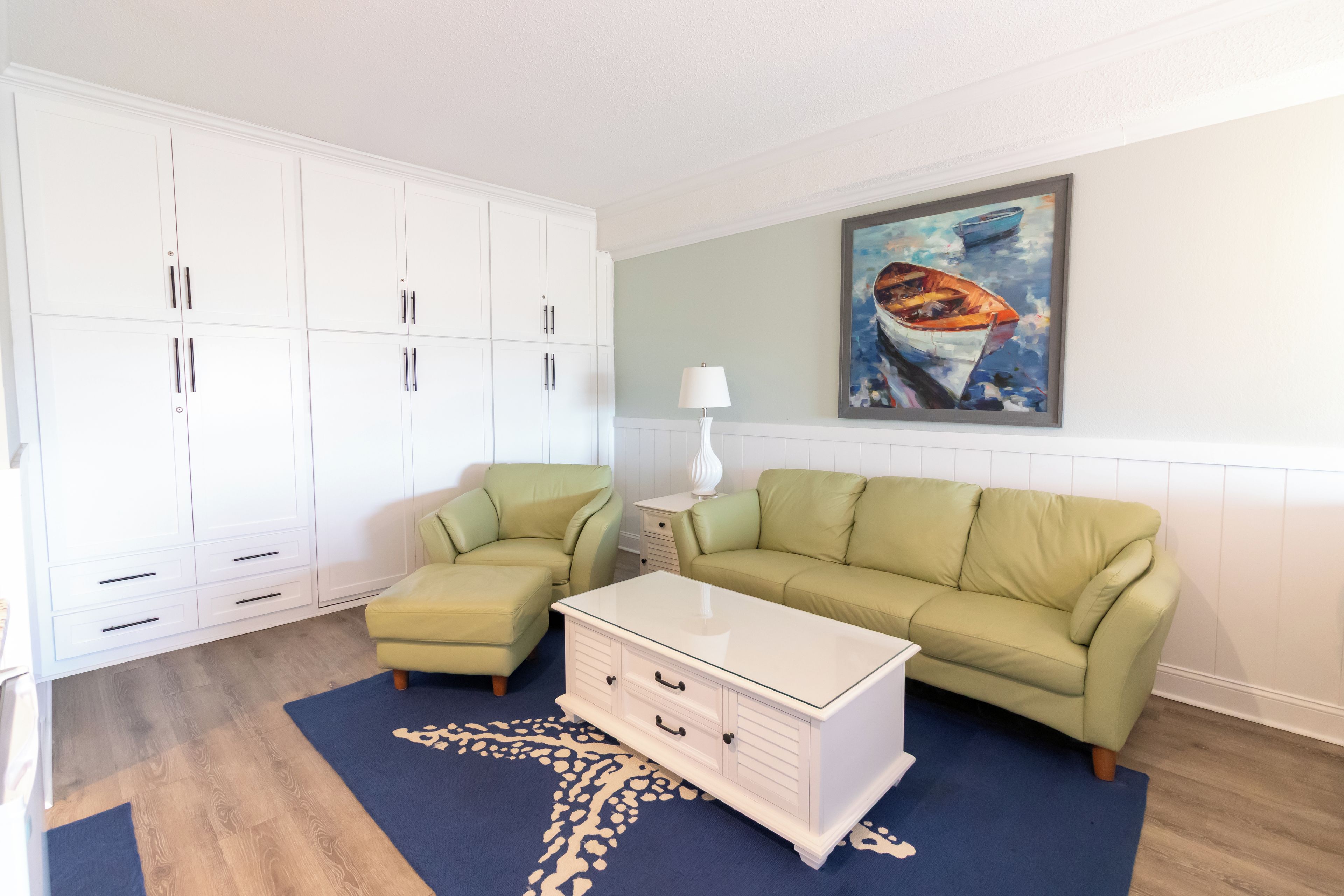 Sala de estar com sofá verde, mesa de centro branca e tapete azul estampado.