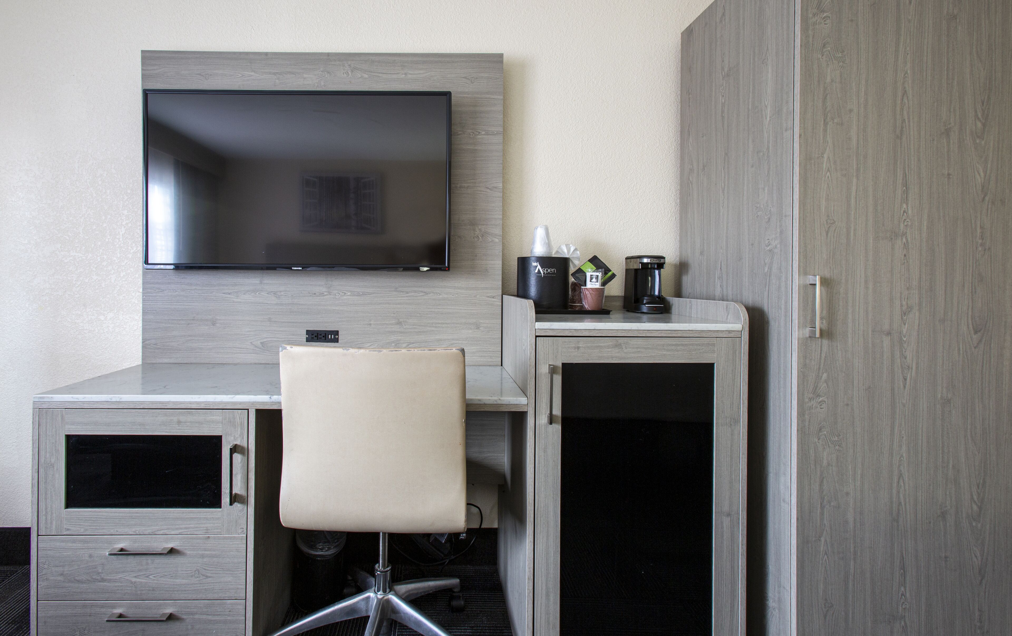 Quarto de hotel com escrivaninha, cadeira, televisão e minibar.