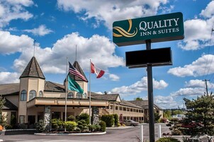 Um hotel com uma placa de destaque que diz 'Quality Inn & Suites', apresentando um estilo arquitetônico tradicional com uma torre e várias bandeiras.