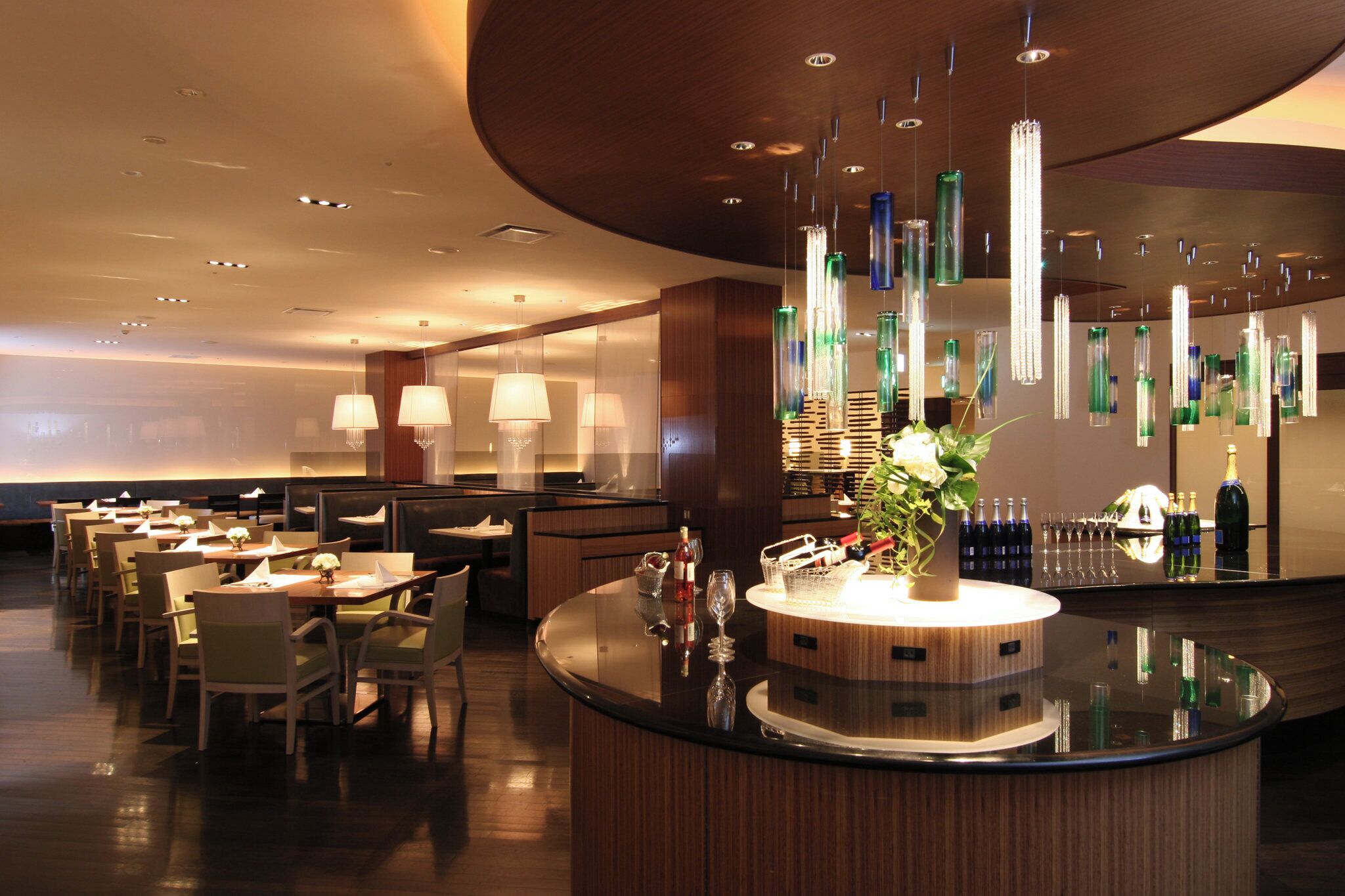 Um restaurante moderno com balcão central, várias mesas de jantar e luminárias pendentes.