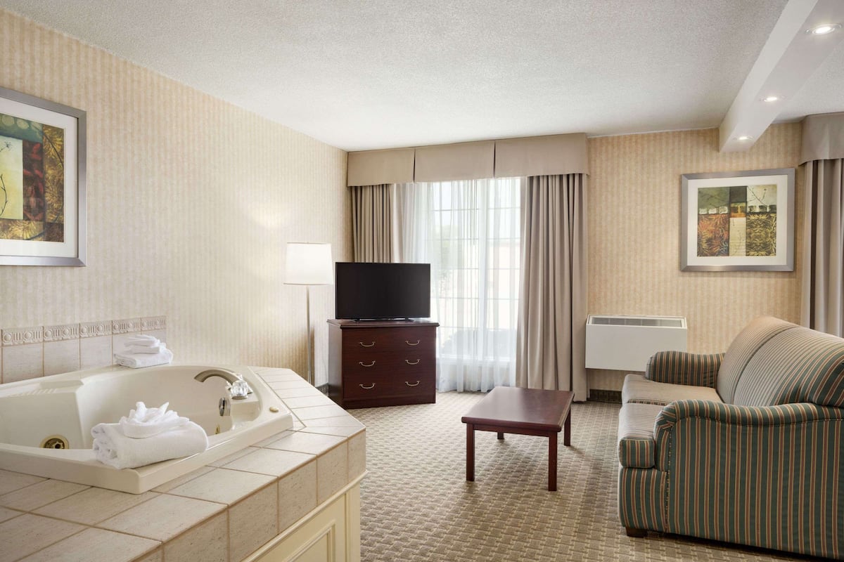 Quarto de hotel com banheira, televisão, sofá e uma mesinha.