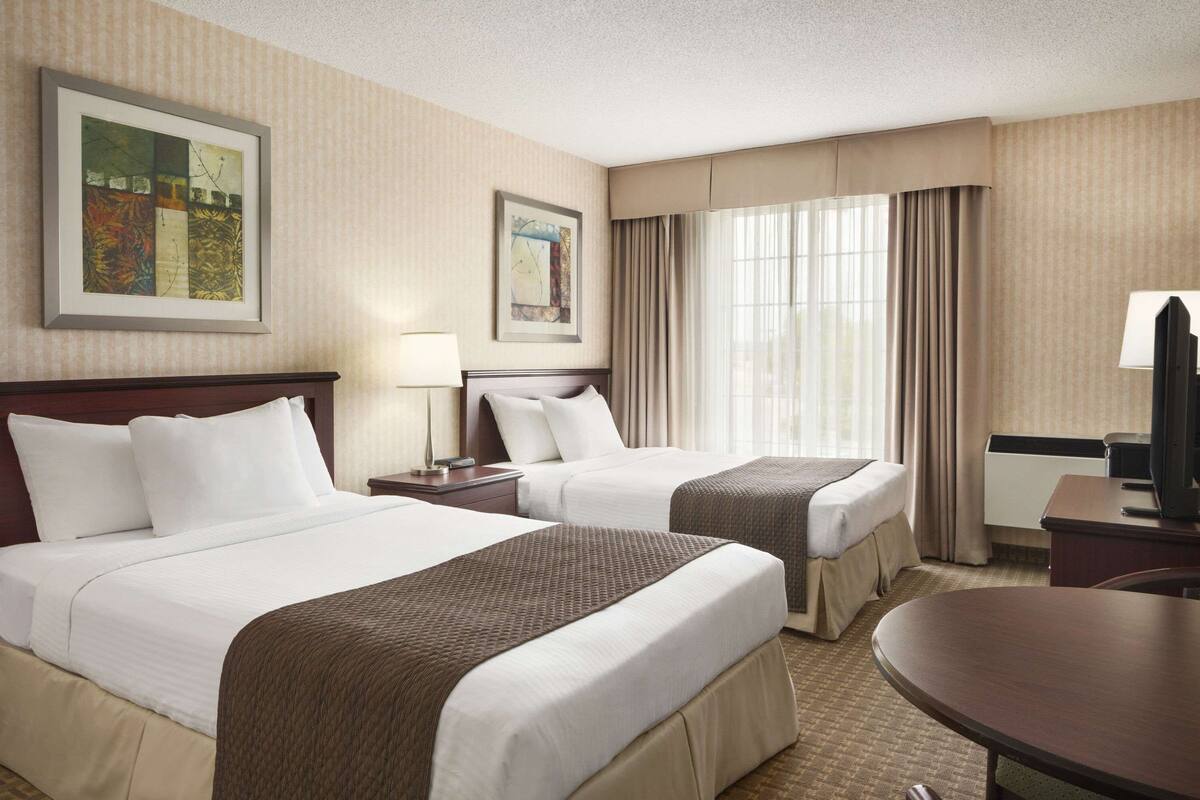 Quarto de hotel com duas camas, uma escrivaninha, uma televisão e uma janela com cortinas.