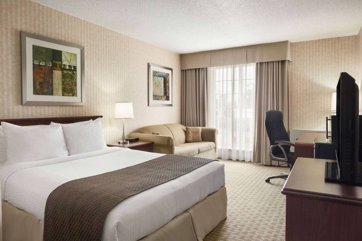 Quarto de hotel com uma cama grande, uma escrivaninha, uma cadeira e uma televisão.