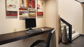 Escritório em casa com uma mesa, computador e três quadros abstratos na parede.
