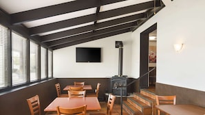 Uma sala de jantar com mesas e cadeiras de madeira, um fogão preto e uma TV fixada na parede.