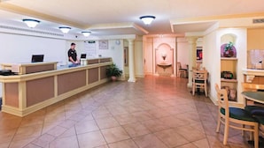 Uma área de recepção com balcão, um homem atrás dele e uma sala de jantar com cadeiras e mesas.