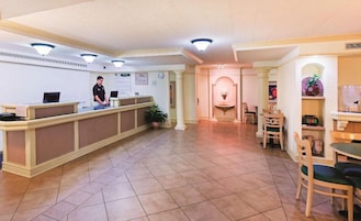 Uma área de recepção com balcão, um homem atrás dele e uma sala de jantar com cadeiras e mesas.
