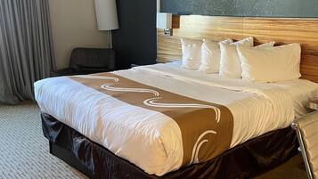 Quarto de hotel com uma cama grande, cabeceira, mesa de cabeceira, abajur e cortina.