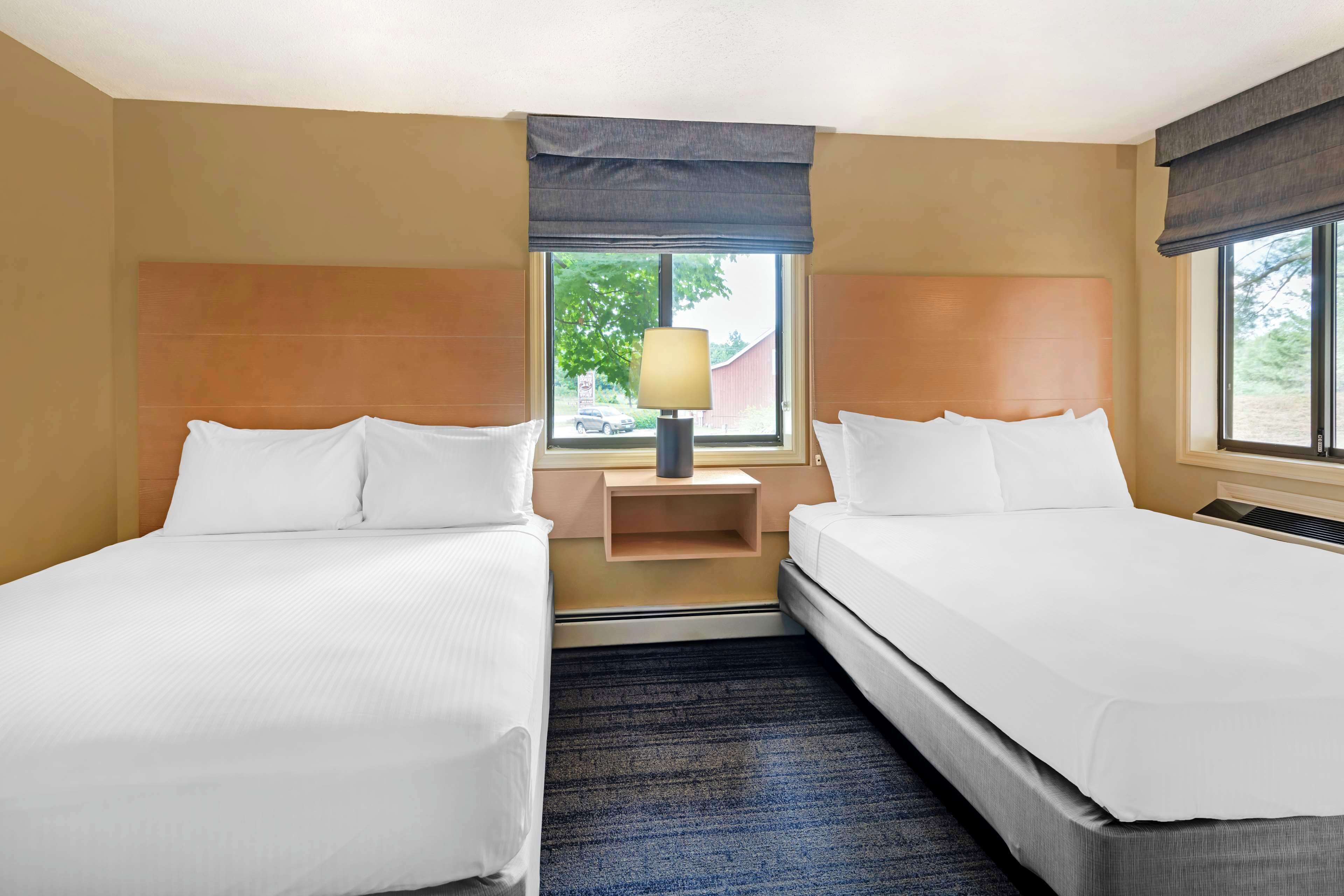 Quarto de hotel com duas camas, mesa de cabeceira, abajur e janela com vista para o exterior.