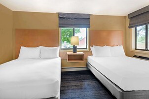 Quarto de hotel com duas camas, mesa de cabeceira, abajur e janela com vista para o exterior.