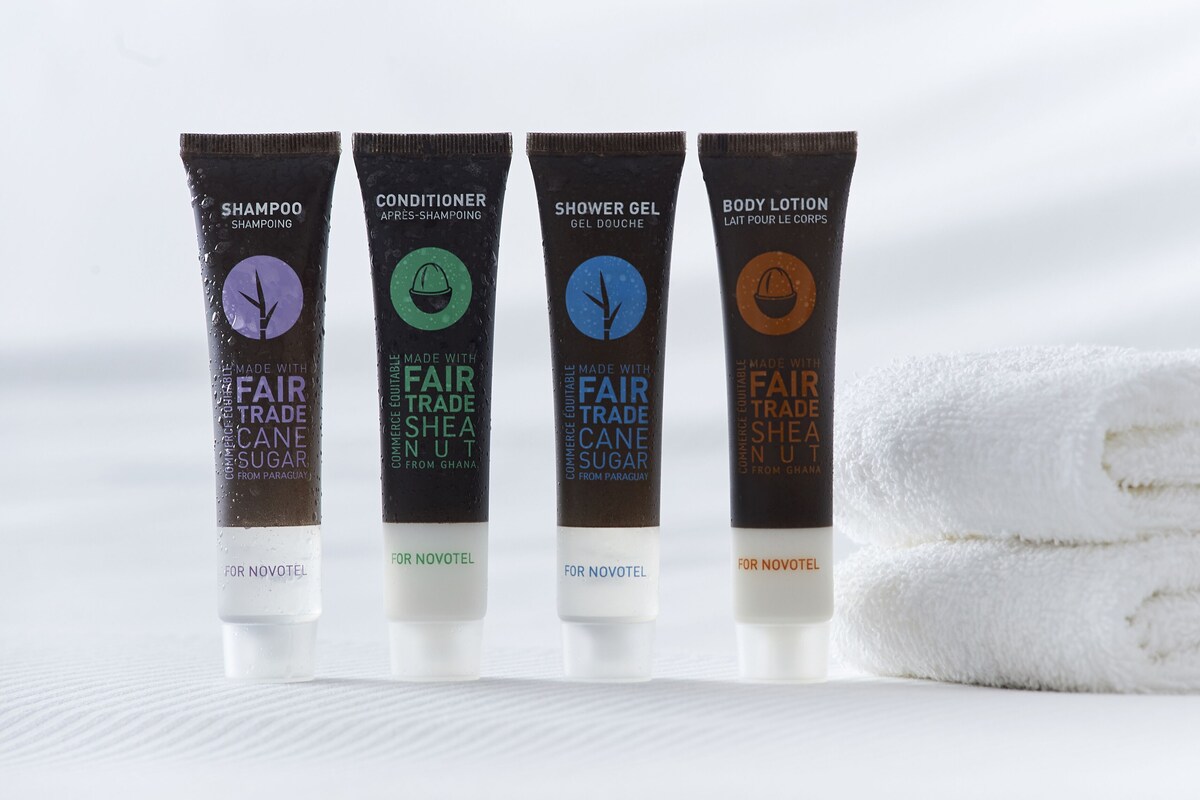 Quatro produtos de higiene: shampoo, condicionador, gel de banho e loção corporal, todos com certificação de comércio justo.