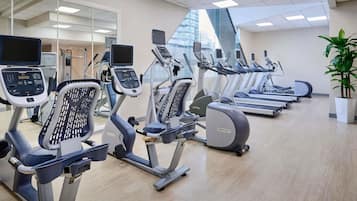 Uma academia com várias máquinas de cardio, um espelho grande e uma planta em vaso.