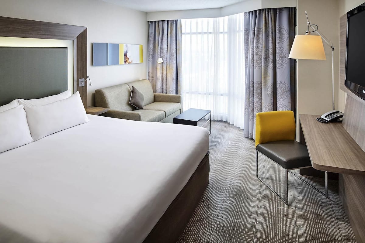 Quarto de hotel com uma cama grande, uma escrivaninha com cadeira, televisão e janela com cortinas.