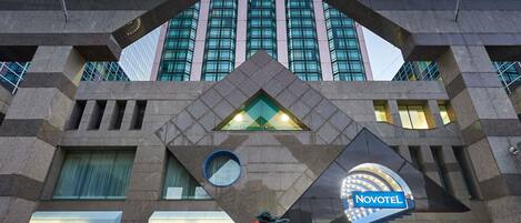 Um hotel com um grande letreiro 'Novotel', design arquitetônico moderno com fachada triangular e uma ampla entrada de vidro.