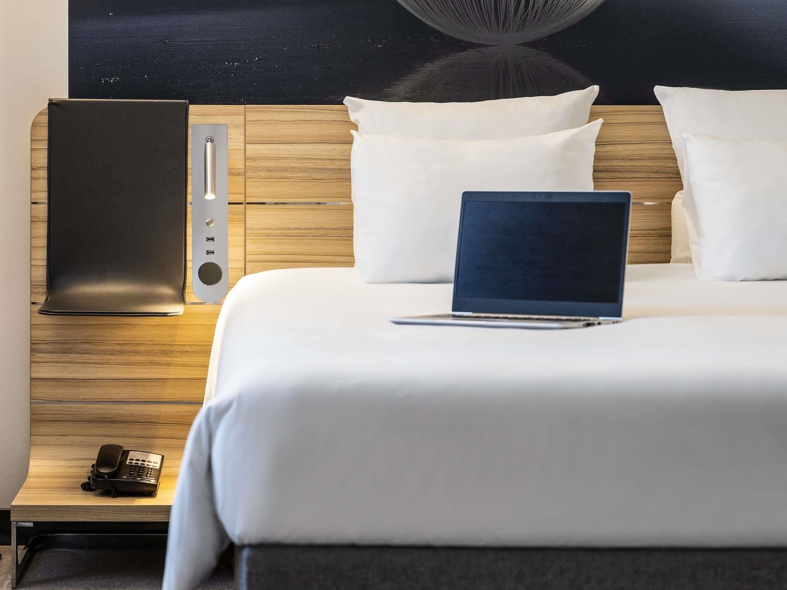 Quarto de hotel com uma cama, um laptop, um telefone e um alto-falante fixado na parede.