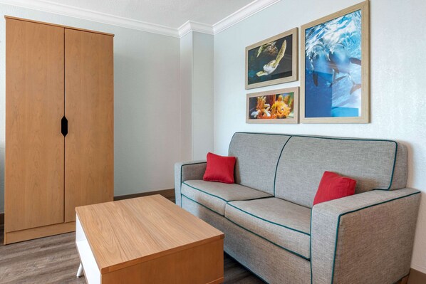 Uma sala de estar moderna com um sofá cinza, duas almofadas vermelhas, uma mesa de centro de madeira e um guarda-roupa grande. Há três quadros na parede.