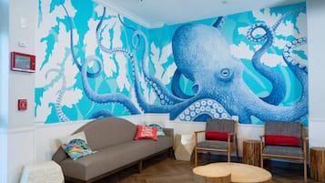 Quarto com um grande mural de polvo, um sofá, duas cadeiras e uma pequena mesa de madeira.