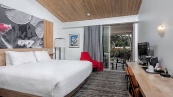 Quarto de hotel moderno com uma cama grande, uma mesa com computador, uma cadeira vermelha e vista para o exterior.
