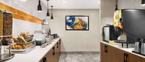 Uma cozinha moderna com bancada branca, luminárias pendentes pretas, uma máquina de café e um quadro grande na parede.