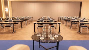Uma sala de conferências com mesas e cadeiras dispostas em fileiras, equipada com garrafas de água e copos.