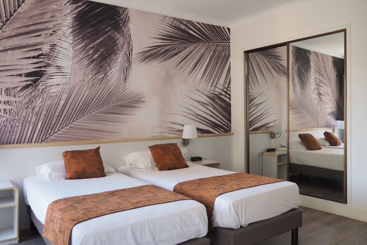 Quarto de hotel com duas camas, um espelho grande e uma parede com padrão de folha de palmeira.