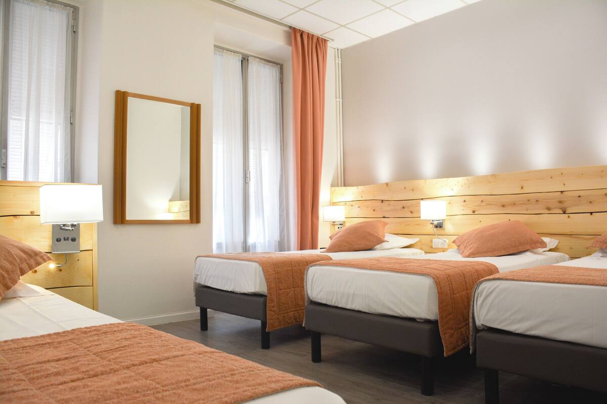 Quarto de hotel com três camas, cabeceiras de madeira e um espelho grande na parede.