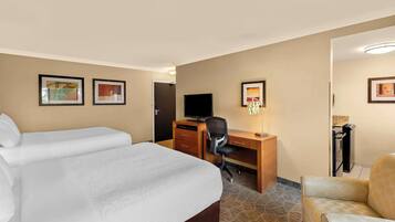 Quarto de hotel com uma cama grande, uma mesa de escritório com um computador, uma cadeira e quadros nas paredes.