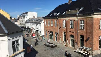 Uma praça de paralelepípedos com edifícios históricos, mesas ao ar livre e uma fonte.