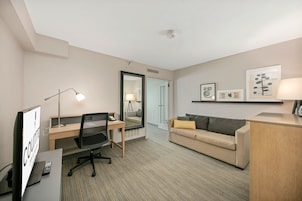 Quarto de hotel com escrivaninha, cadeira de escritório e sofá com almofada decorativa.